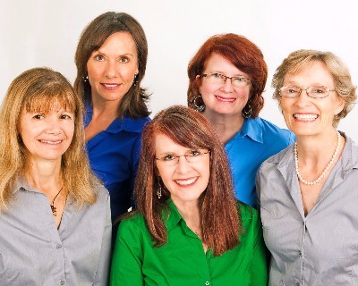 Five professional women posing together, smiling warmly at the camera ...